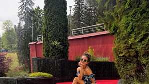 Mulher sentada em degraus vermelhos em um jardim com diversas plantas e flores.