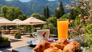 Mesa com croissants, um copo de sumo de laranja e uma chávena, montada ao ar livre com vista para a montanha.