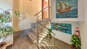 Uma escada com guarda-corpos de metal, uma porta que dá para outro cômodo e dois quadros pendurados na parede, representando um veleiro e golfinhos.