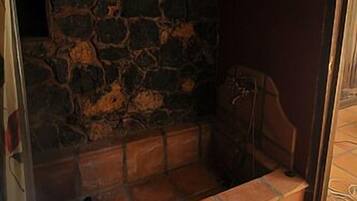 Casa de banho com paredes de pedra, chão em mosaico e porta de madeira.