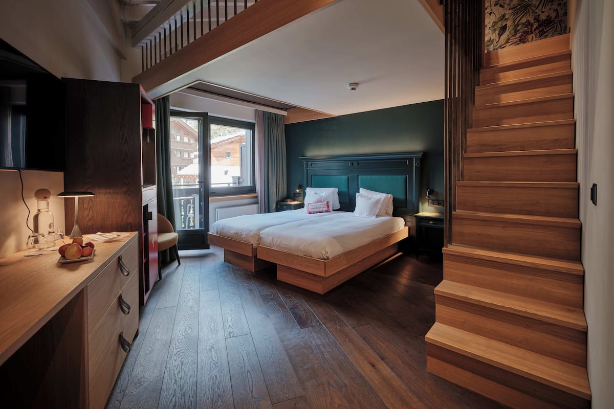 Quarto moderno com cama grande, piso de madeira e escada.