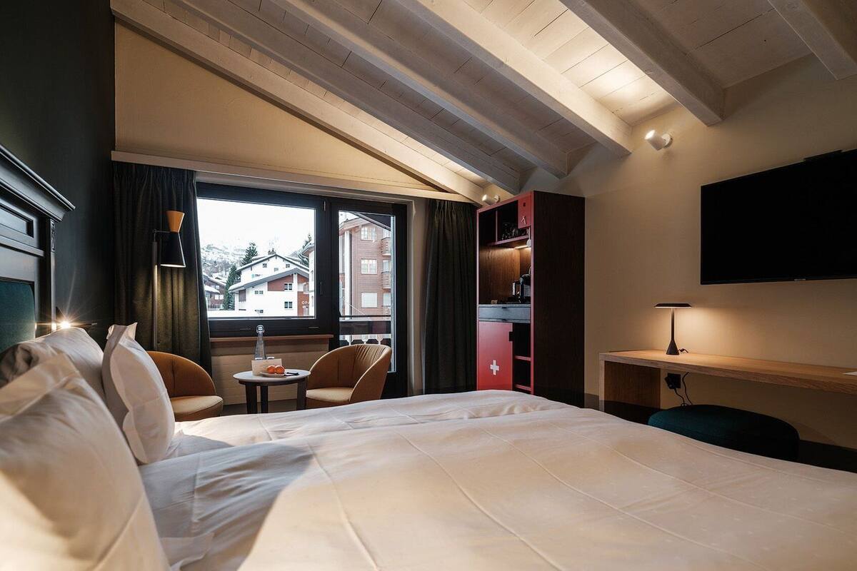Quarto de hotel com uma cama grande, uma escrivaninha com cadeira, televisão e janela com vista para edifícios.