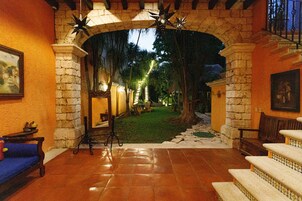 Um pátio interno com paredes de pedra, chão de azulejos e um banco de madeira.