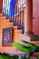 Uma escadaria com grades pretas elaboradas e um pilar, que leva a um quarto com um quadro na parede.