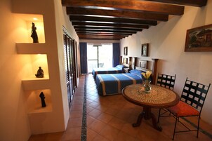 Quarto de hotel com cama, mesa de jantar, cadeiras e uma pequena estatueta numa estante.