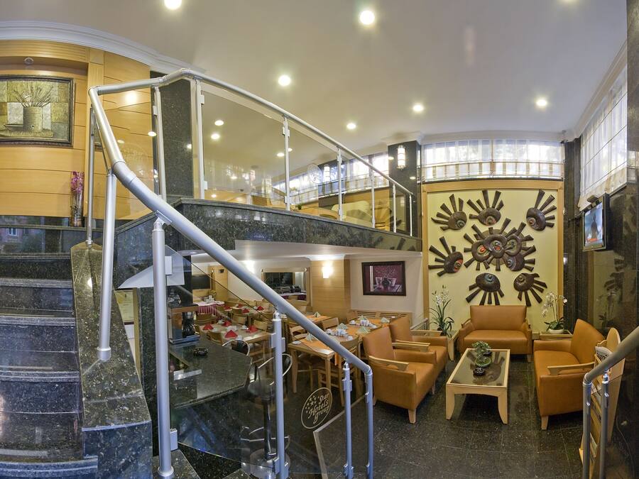 Um amplo saguão com escadarias de mármore, área de estar com poltronas de couro e um mural decorativo.