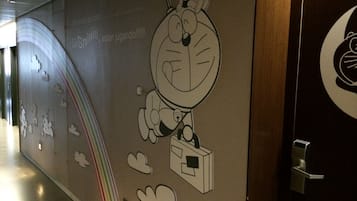 Um corredor com ilustração de personagem de desenho animado na parede, uma porta com logotipo circular e um desenho de arco-íris no chão.