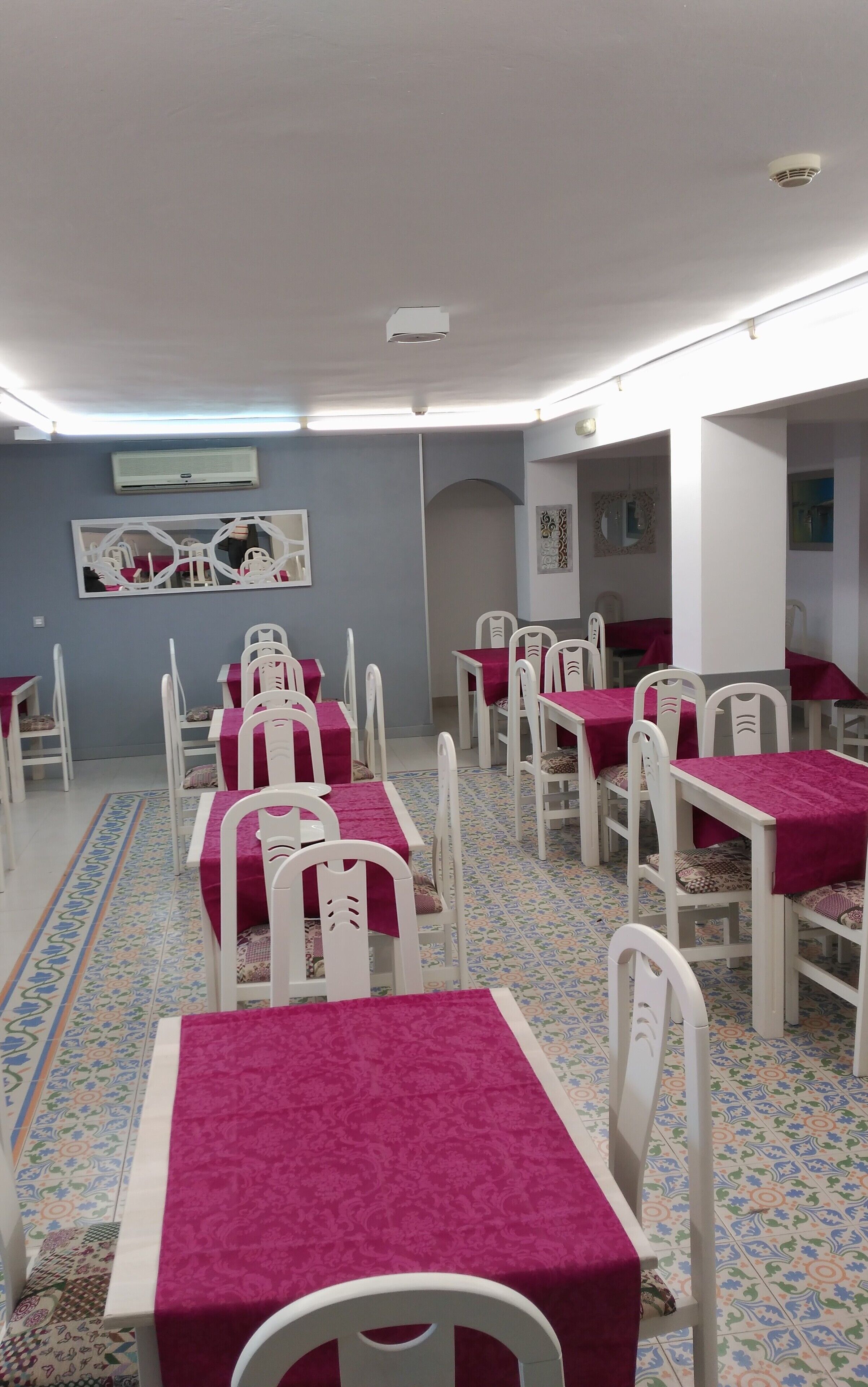 Uma sala de jantar com cadeiras e mesas brancas, cada uma coberta por uma toalha rosa.