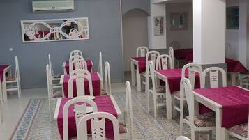 Uma sala de jantar com cadeiras e mesas brancas, cada uma coberta por uma toalha rosa.