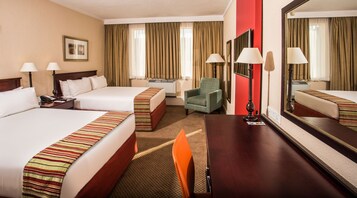 Quarto de hotel com duas camas, uma escrivaninha, uma cadeira e um espelho grande.