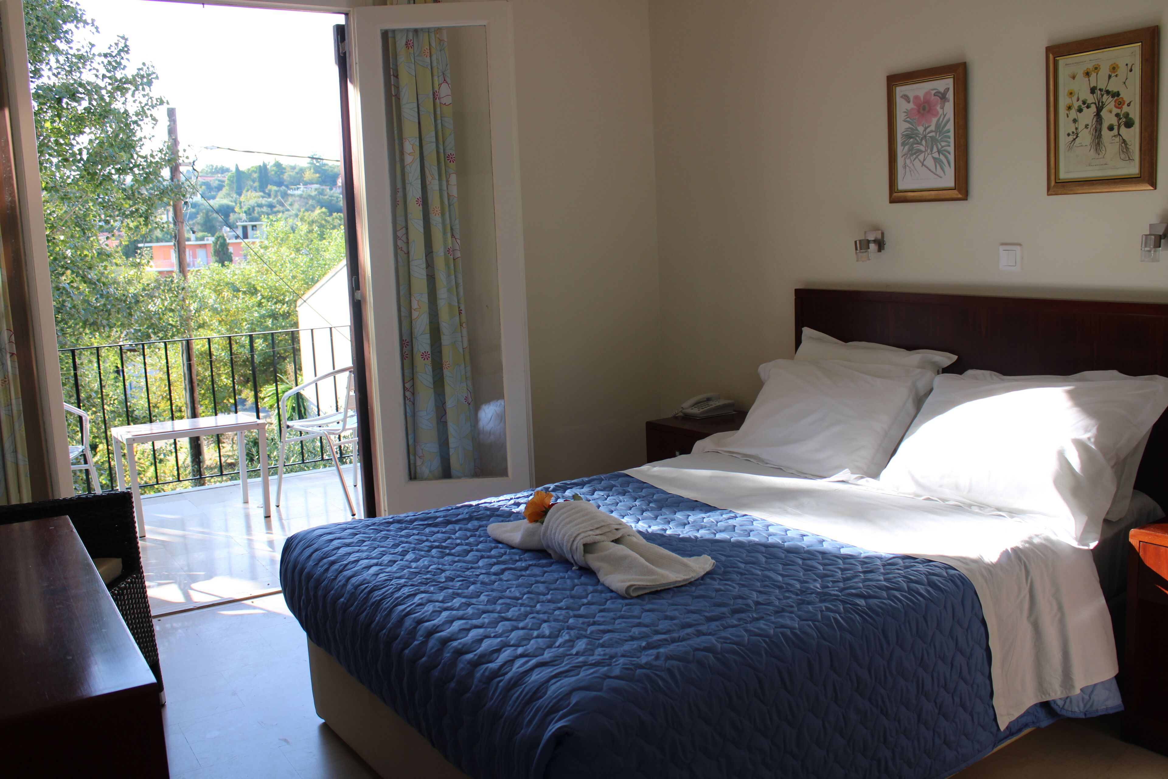 Quarto de hotel com cama, mesa de cabeceira, escrivaninha e varanda com vista para a cidade.