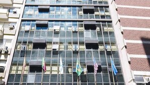 Exterior do Hotel Copacabana Mar, com diversas bandeiras, uma entrada imponente e o número do prédio visível.