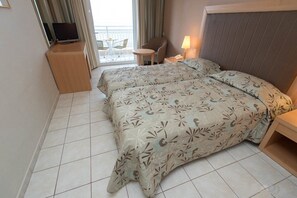Quarto de hotel com duas camas, televisão, mesinha, cadeira e vista para a varanda.
