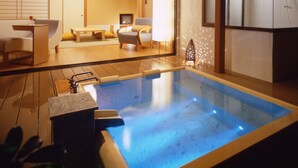 Quarto de hotel moderno com uma piscina ampla e bem iluminada, piso de madeira e área de estar com televisão.