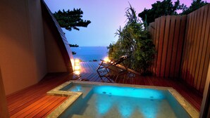 Uma banheira de hidromassagem com um deck de madeira e vista para o oceano ao entardecer.