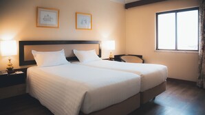 Uma cama de casal com cabeceira de madeira, duas mesas de cabeceira com luminárias, uma cadeira e uma janela com cortinas.