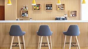 Uma área de bar com painéis de madeira, três banquetas e prateleiras com garrafas.