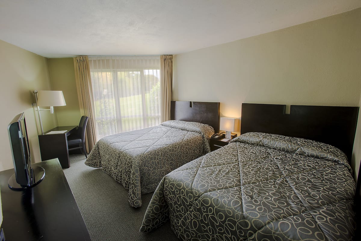Quarto de hotel com duas camas, uma escrivaninha, uma cadeira e uma televisão.