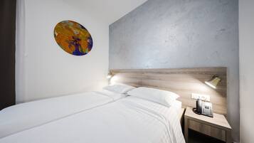Quarto de hotel com uma cama grande, mesa de cabeceira com telefone e um quadro pendurado na parede.