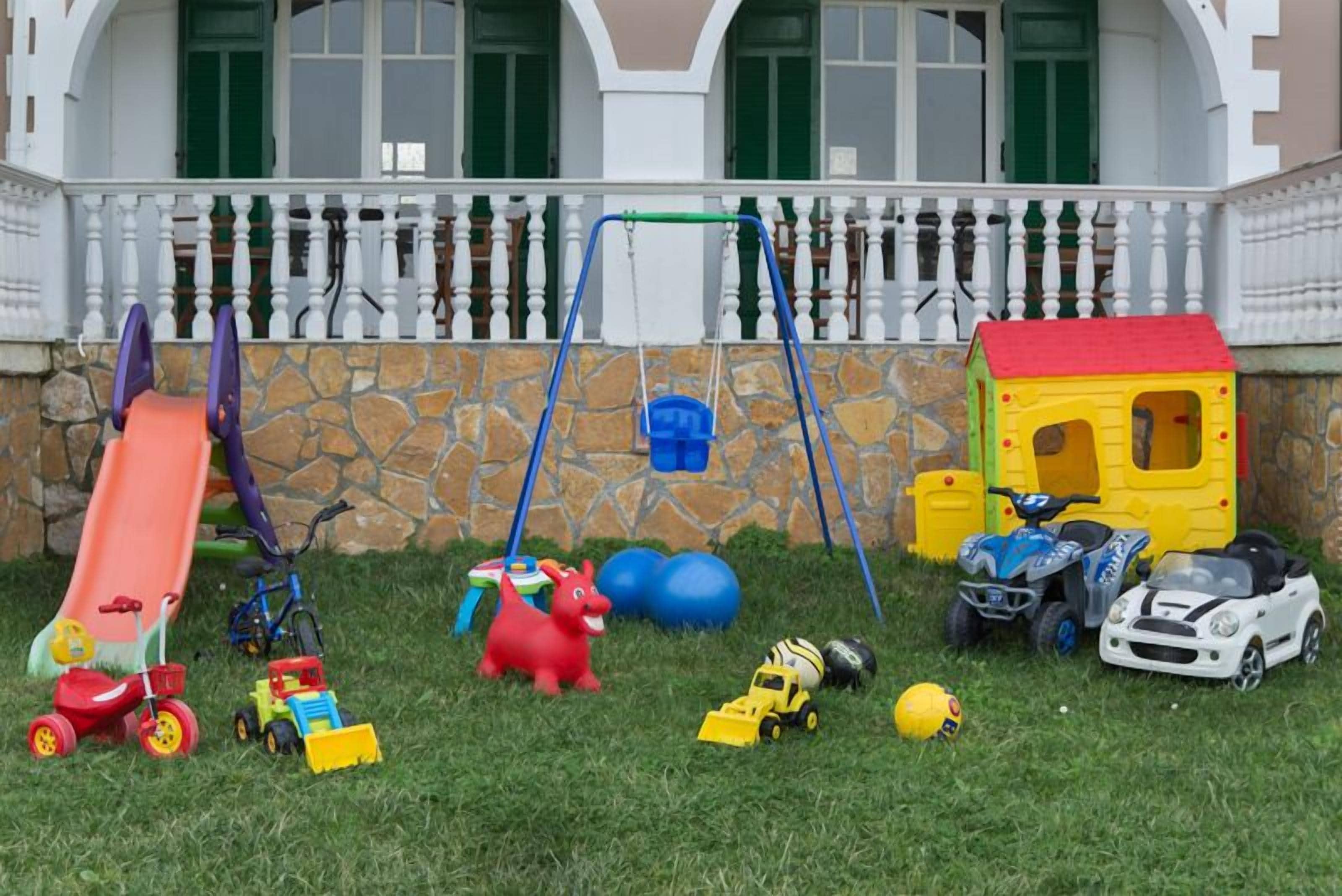 Uma área de recreação infantil com escorrega, baloiço, veículos de brinquedo e uma casinha.