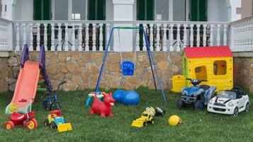 Uma área de recreação infantil com escorrega, baloiço, veículos de brinquedo e uma casinha.