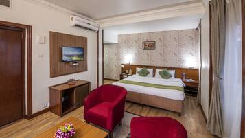 Quarto de hotel com uma cama, televisão, escrivaninha e duas cadeiras vermelhas.