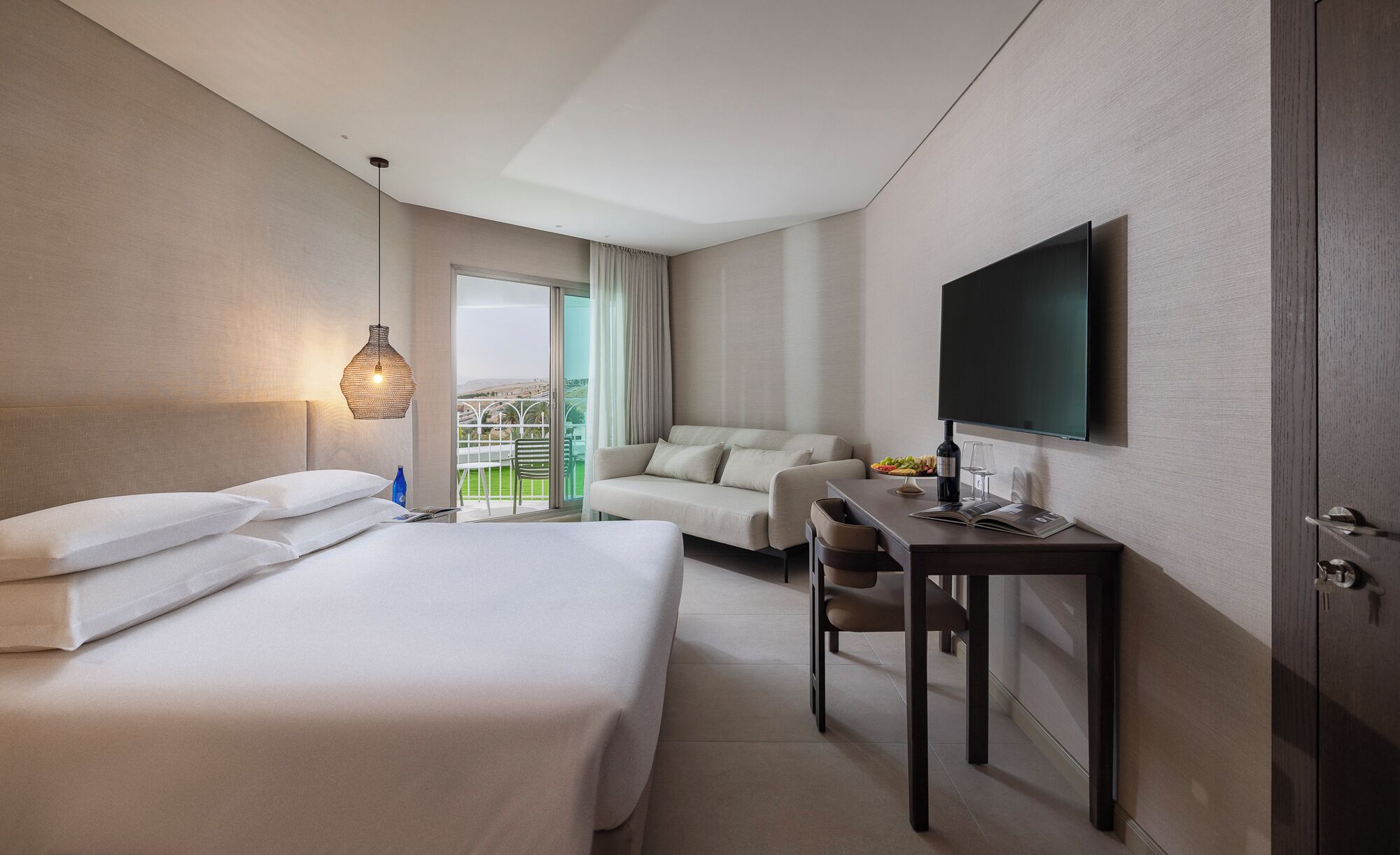 Quarto de hotel com cama, escrivaninha, televisão e varanda com vista.