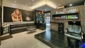 Interior moderno de salão com balcão de recepção, sofá de couro preto, estação de lavagem de cabelo e prateleiras com produtos para cabelo.
