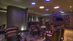 Uma área de bar com assentos de couro, balcão e uma tela de televisão.