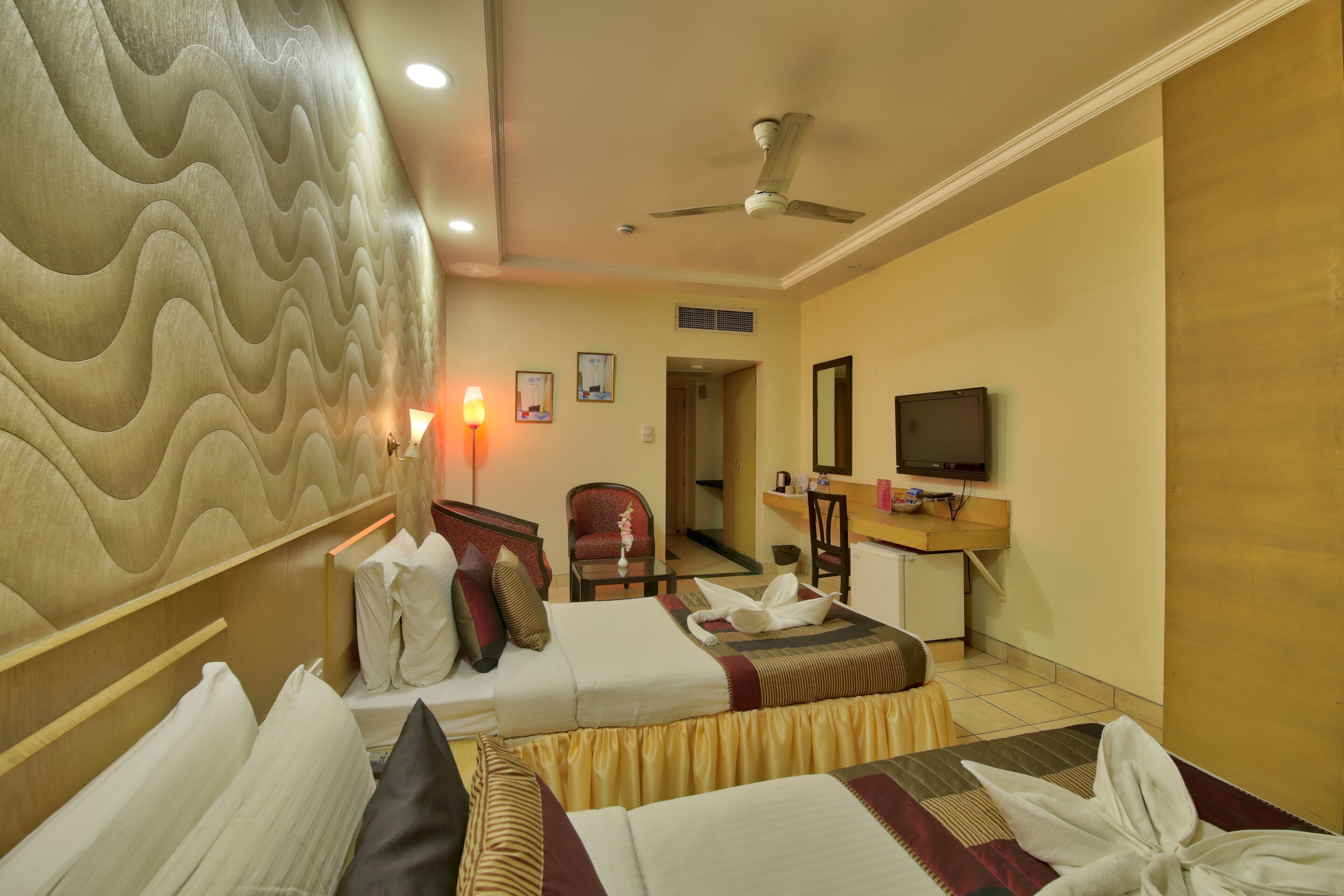 Quarto de hotel com duas camas, uma escrivaninha com televisão, uma cadeira e um abajur.
