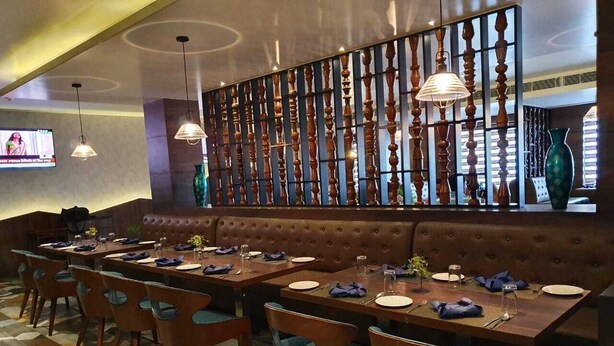 Restaurante com uma longa mesa de madeira preparada para refeições, assentos acolchoados e iluminação pendente.