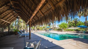 Uma área de piscina com espreguiçadeiras e uma cobertura de palha.