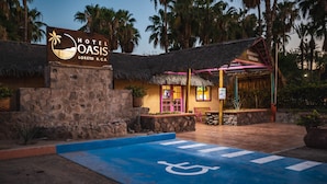 Um hotel chamado Hotel Oasis com telhado de palha, uma placa e uma vaga de estacionamento acessível azul.