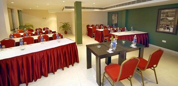 Uma sala de conferência com várias mesas e cadeiras, garrafas de água e um vaso de planta.