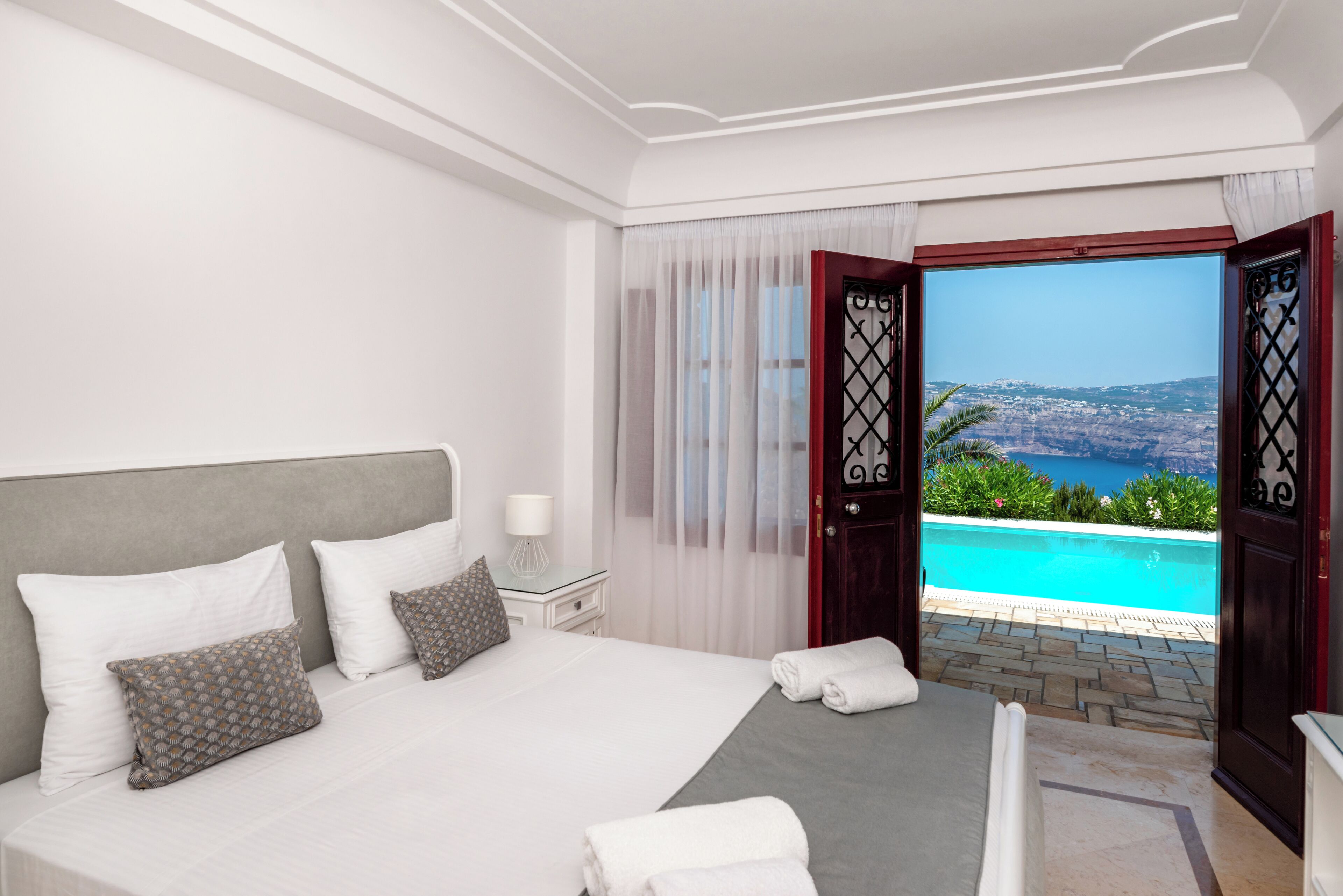 Quarto de hotel com cama, mesa de cabeceira, abajur e vista para a piscina e paisagem.