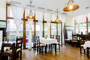 Restaurante com piso de madeira, toalhas brancas nas mesas e luminárias pendentes.