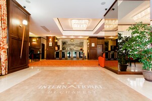 Um hall de hotel com piso de mármore, balcão de recepção, um candelabro e uma grande planta em vaso.