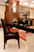 Um piano num quarto com um armário de madeira, um relógio na parede e um quadro emoldurado.