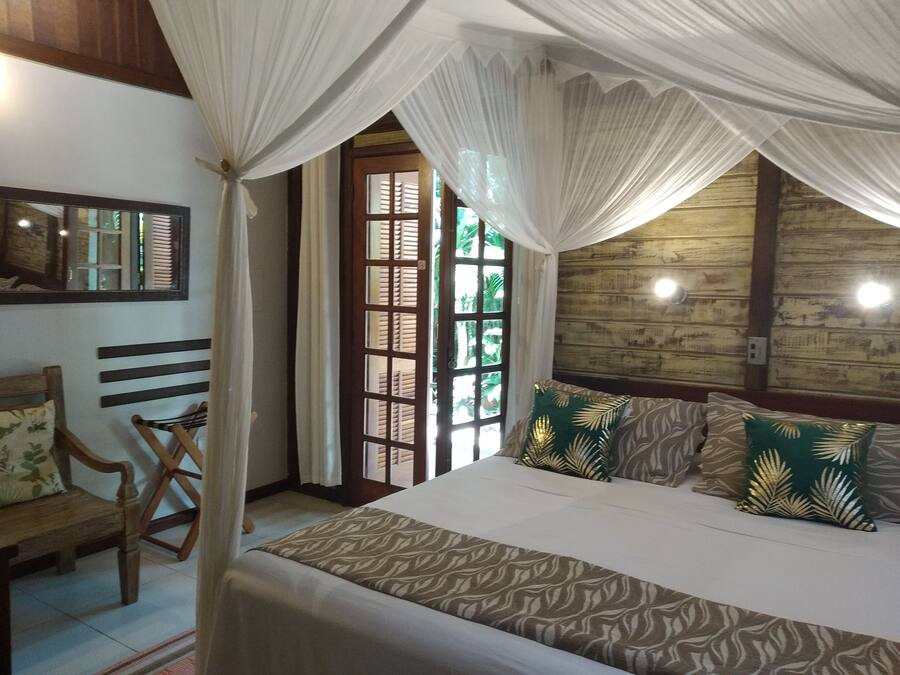 Quarto com cama, cadeira, espelho e janela com cortinas.