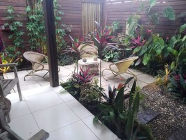 Uma área de pátio com móveis de vime, piso de azulejos e diversos vasos de plantas.