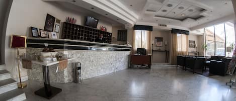 Um hall espaçoso com uma receção em mármore, lareira e área de estar com cadeiras e uma mesa.