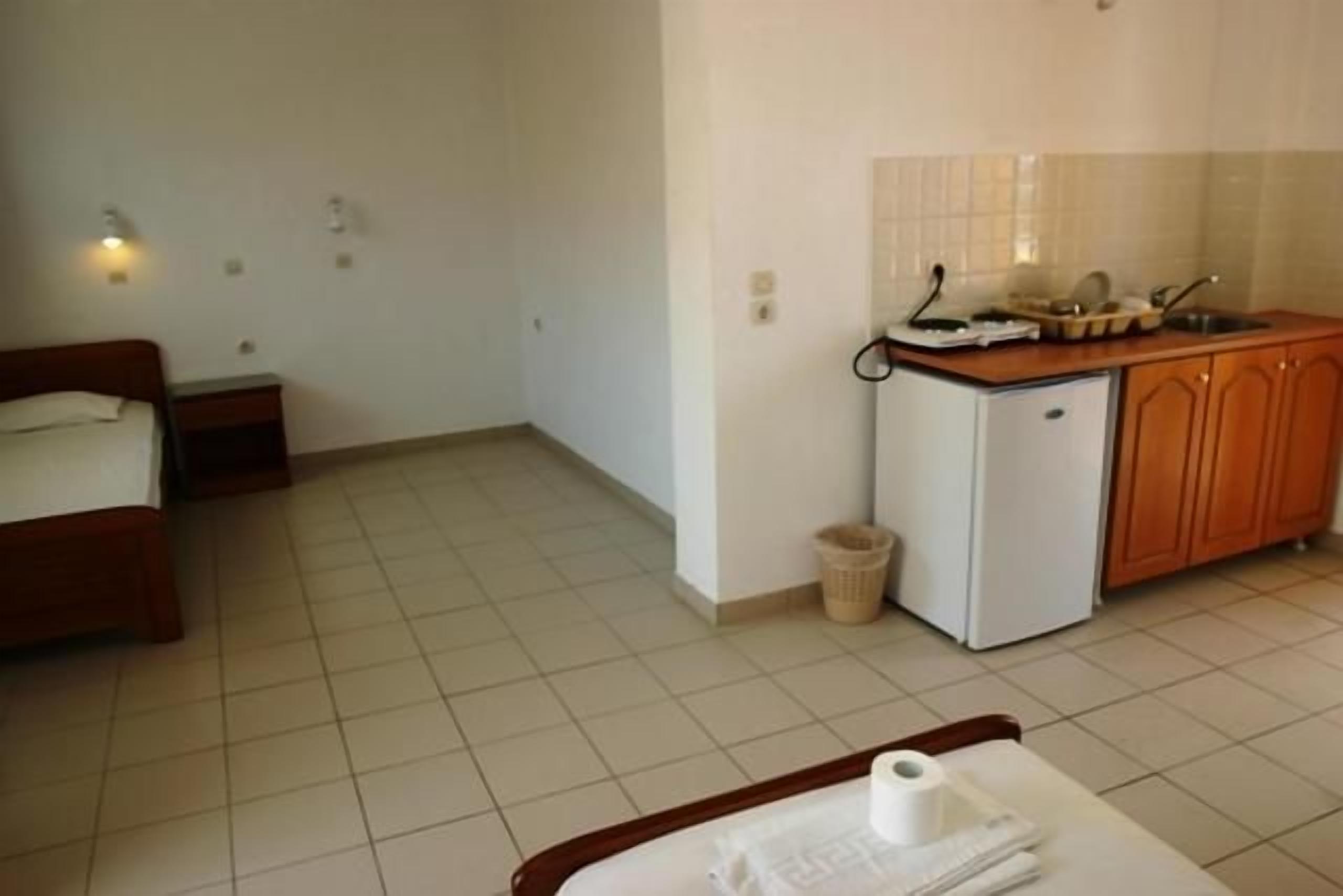 Quarto compacto com uma cama, pequeno espaço de cozinha e um cesto de lixo.