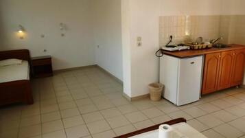 Quarto compacto com uma cama, pequeno espaço de cozinha e um cesto de lixo.