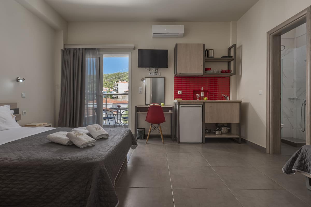 Quarto de hotel com cama, escrivaninha, cozinha compacta e banheiro.