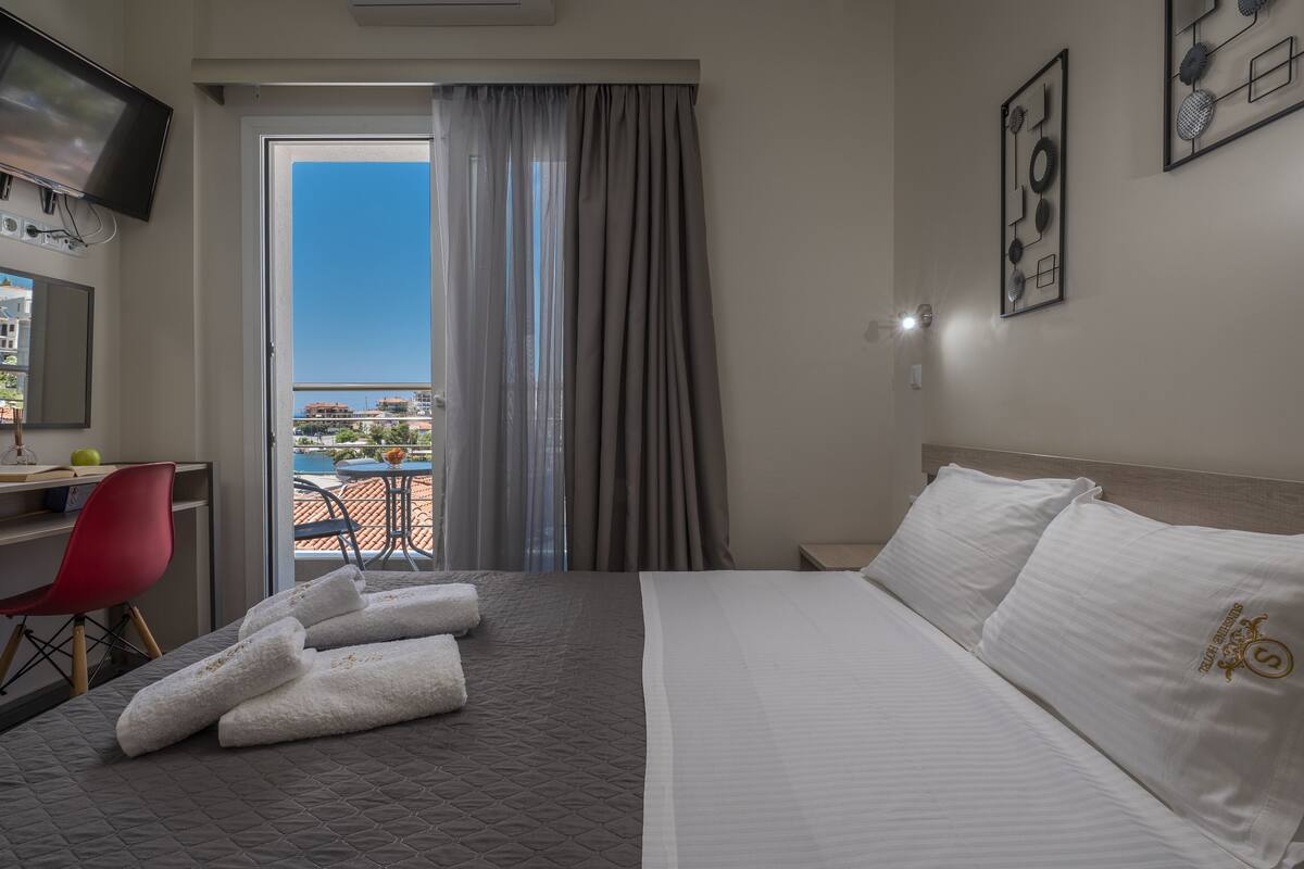 Quarto de hotel com cama, escrivaninha, cadeira e vista para o exterior.