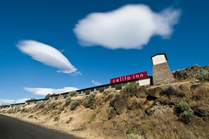 Um hotel chamado 'celilo inn', com design moderno, localizado numa encosta sob um céu azul límpido e vegetação escassa.