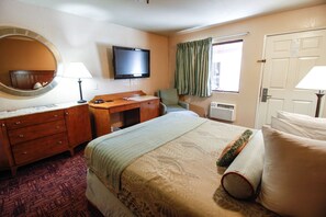 Quarto de hotel com cama, escrivaninha, cadeira, televisão, espelho e janela com cortinas.