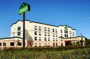 Um hotel com uma placa verde indicando "Wingate by Wyndham". Apresenta um edifício de vários andares com fachada branca e detalhes verdes.