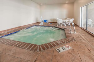 Uma piscina interior com borda revestida, uma cadeira azul e cadeiras brancas em volta de uma mesa.