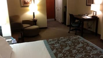 Quarto de hotel com cama, escrivaninha, duas cadeiras, abajur e porta que dá para outro espaço.